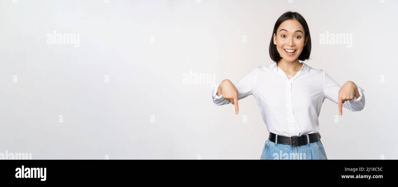 Portrait of young asian woman pointing fingers down and smiling ...