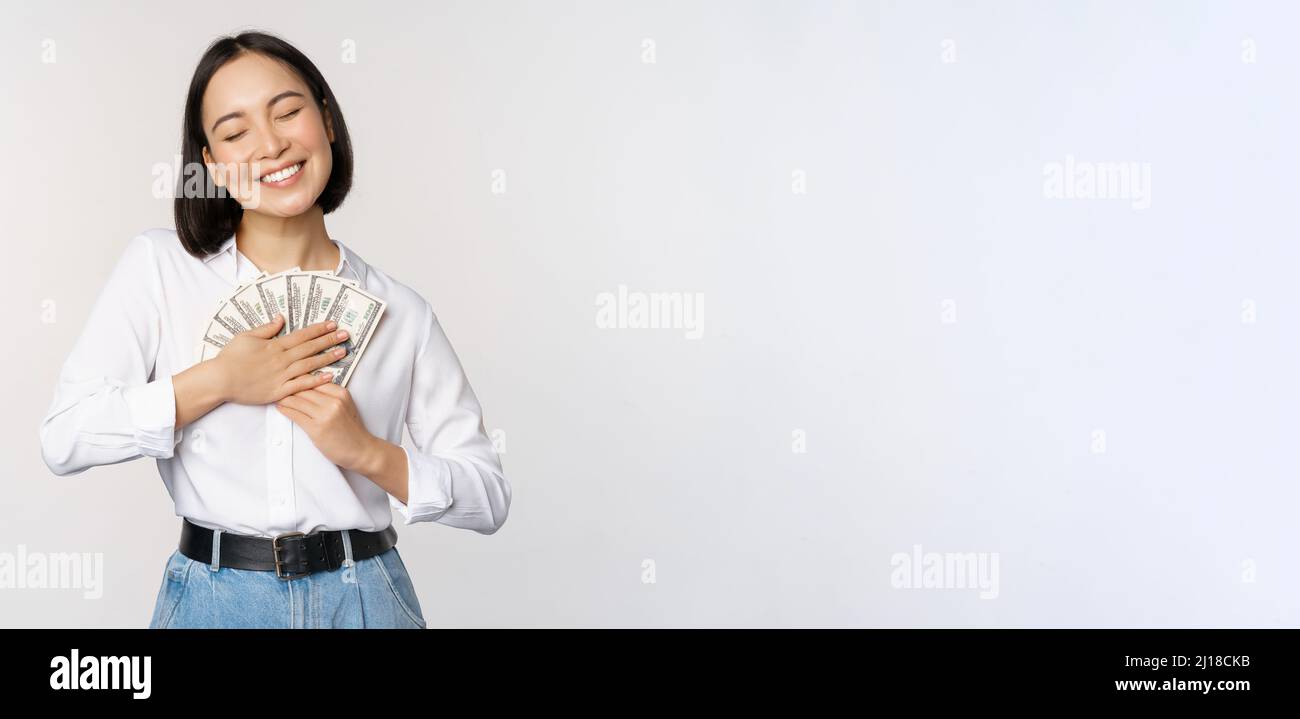 Happy asian woman hugging money dollars and smiling satisfied, standing ...