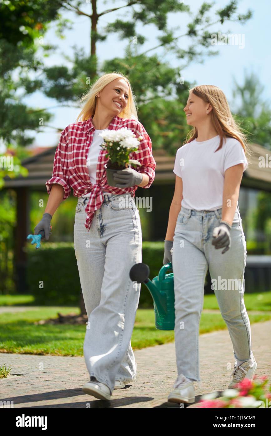 Positive teenage girl walking with her pleasant mother at garden with ...