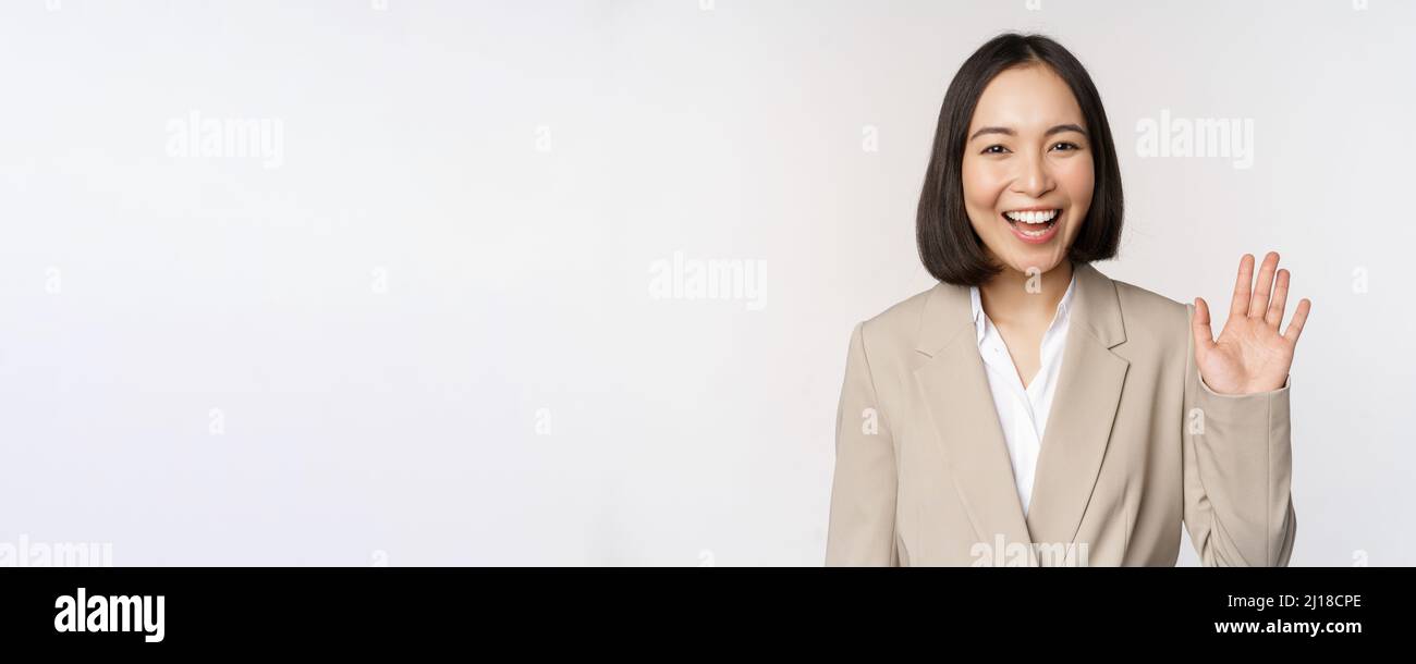 Friendly business woman, asian office lady waving hand and saying hello ...