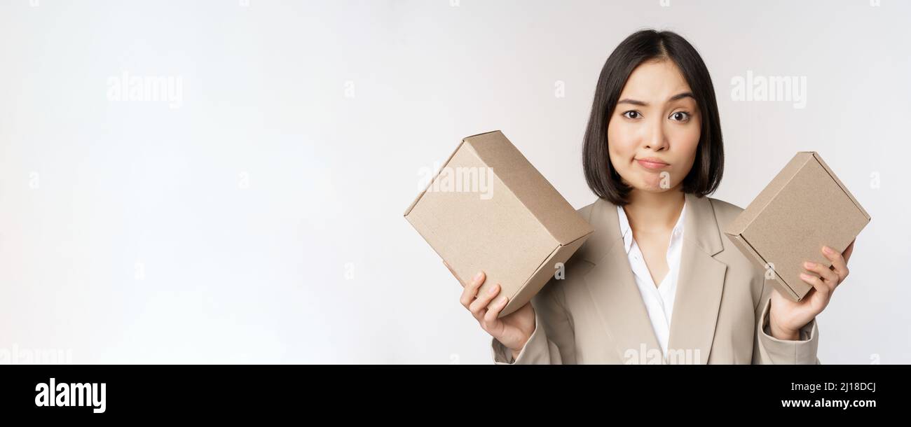 Puzzled asian saleswoman holding boxes, looking confused, standing in ...