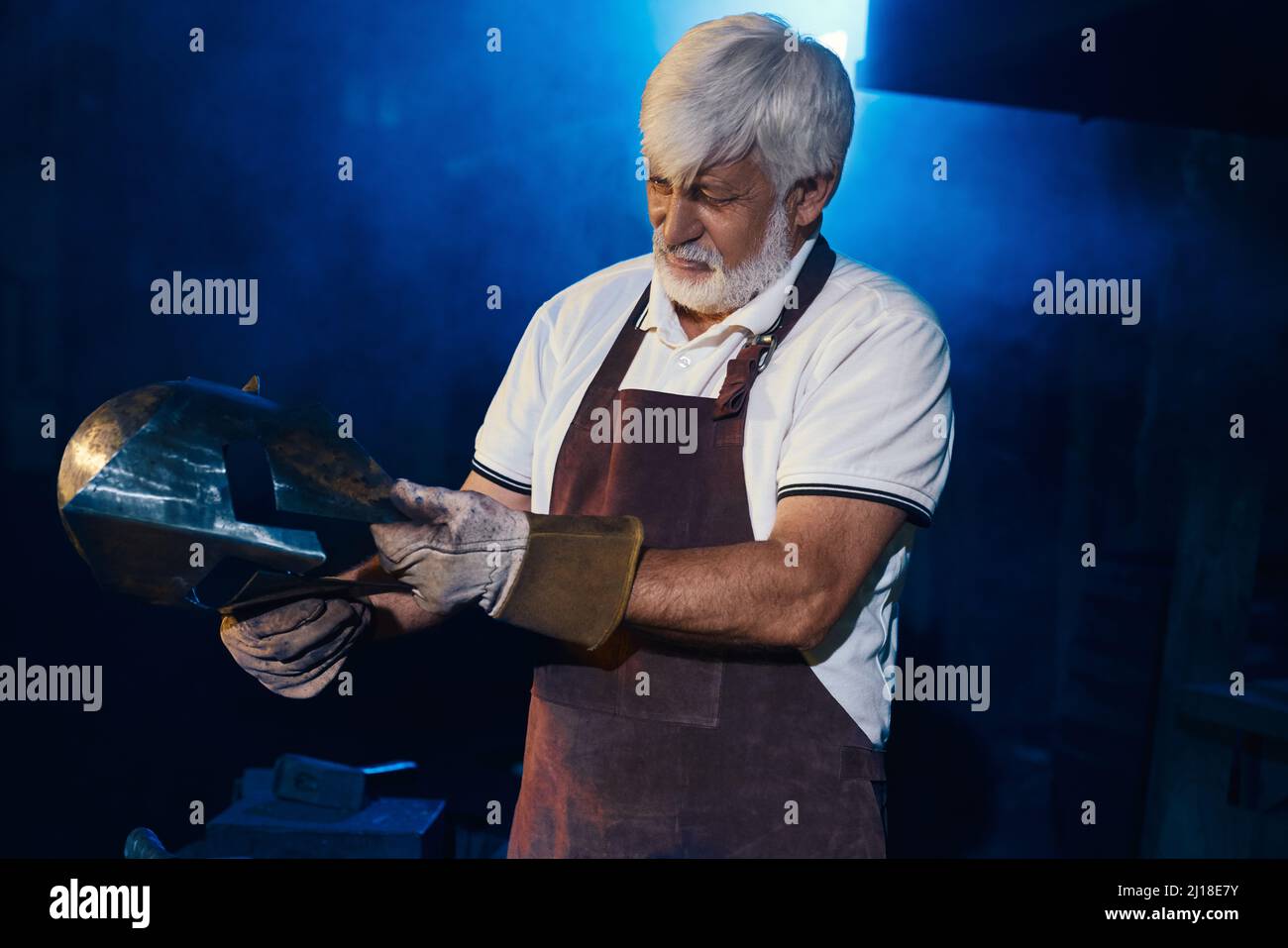 Mature caucasian standing at forge and holding gladiator helmet in ...