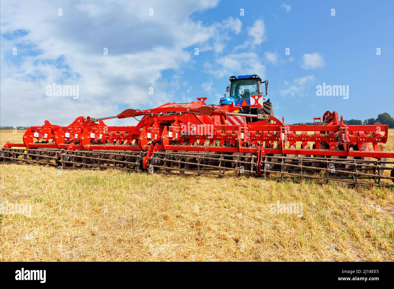 A red multifunctional agricultural harrow stands as a hitch on an ...