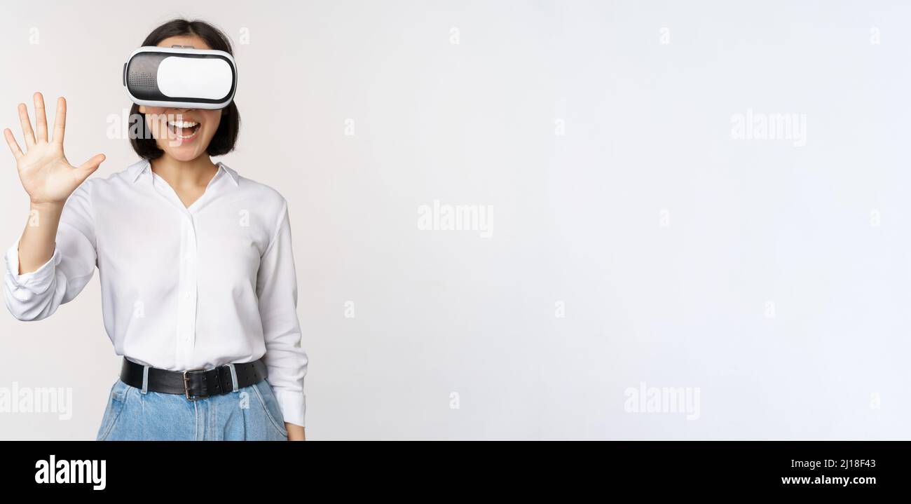 Smiling asian woman waving at you, wearing virtual reality glasses, vr ...