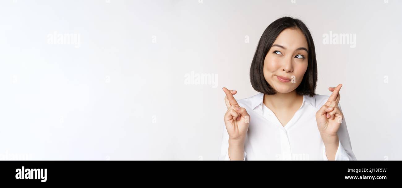 Hopeful young lucky girl making wish, cross fingers and looking aside ...