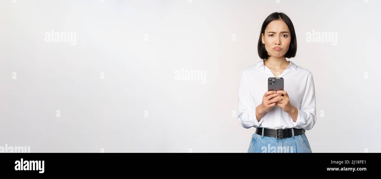 Asian woman holding smartphone and looking with doubt, disappointed ...