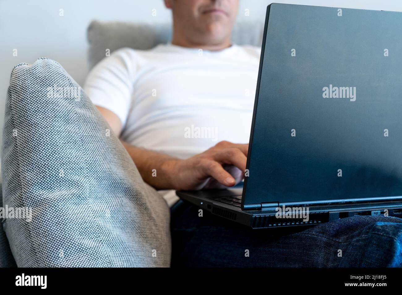 Foreground on unrecognizable man sitting in an armchair using a laptop ...