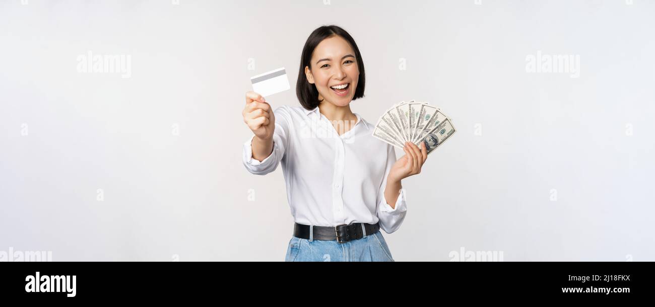 Happy korean woman holding credit card and money dollars, smiling and ...