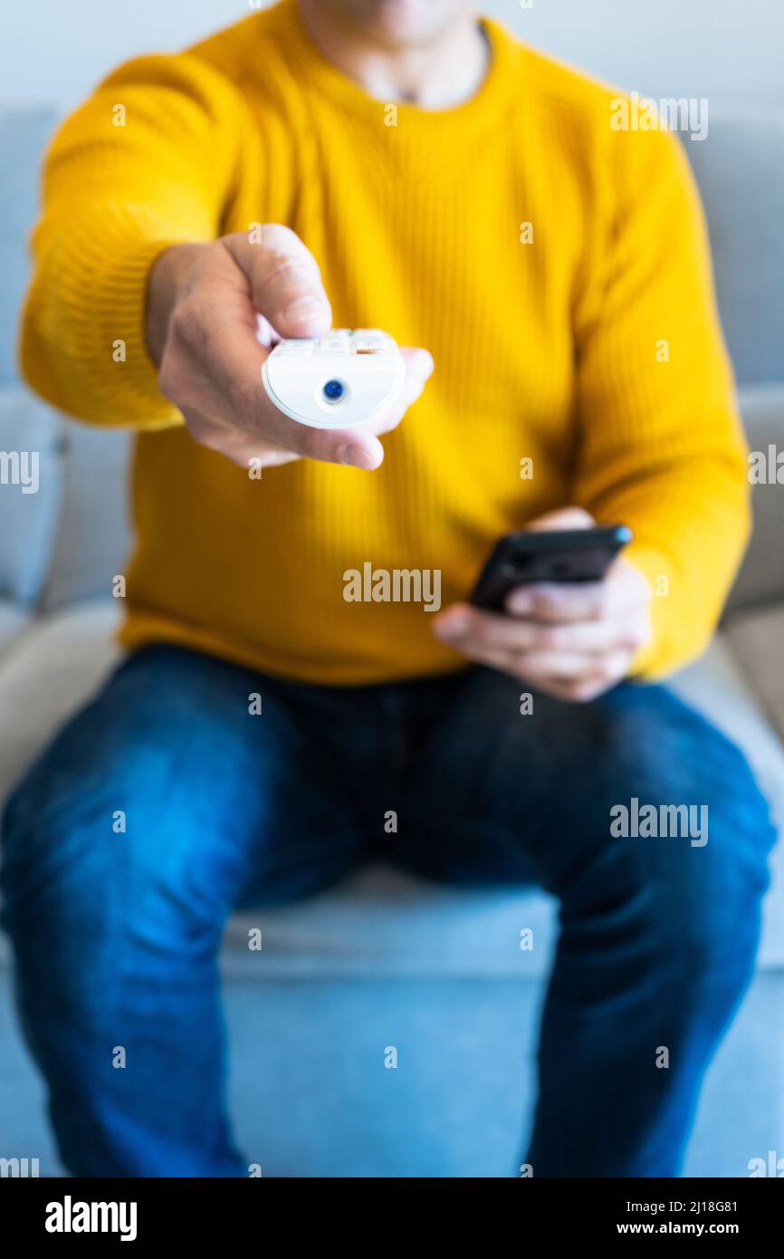 Unrecognizable man pointing to the camera with TV's remote control ...