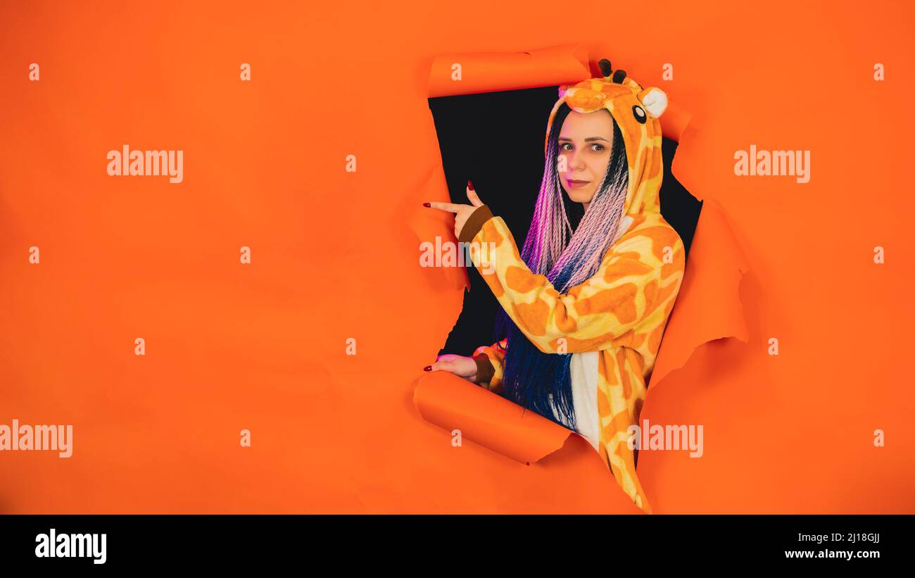 Young woman in pajamas of giraffe sticking out of hole of orange ...