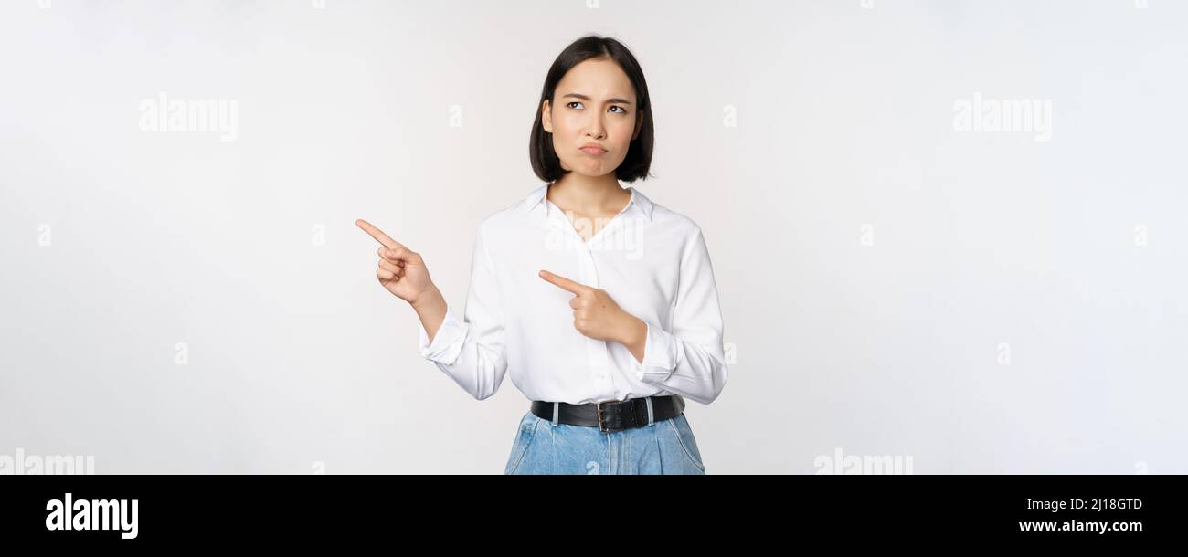 Disappointed, sad young asian woman pointing and looking left with ...