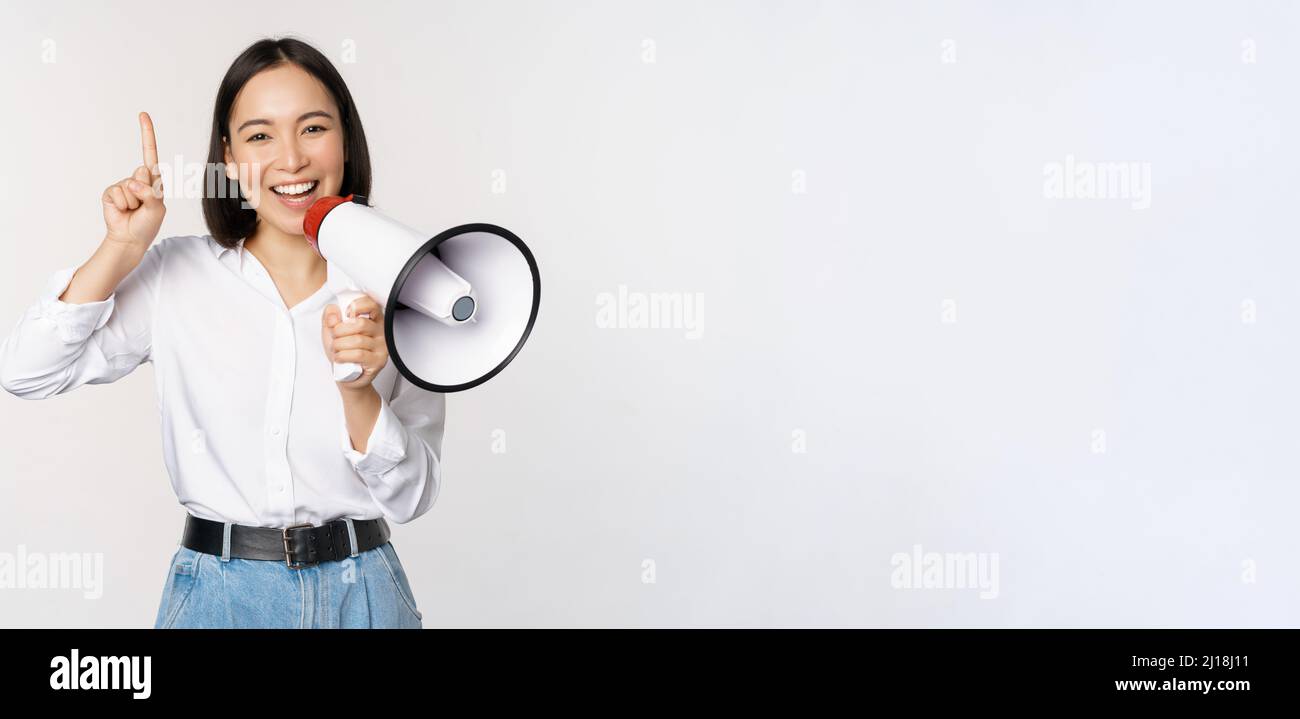 Smiling happy asian girl talking in megaphone and pointing up ...
