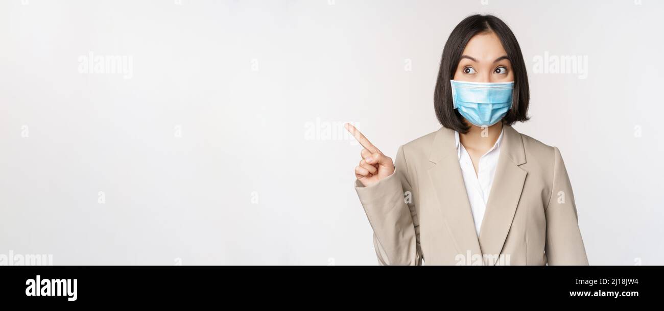Enthusiastic businesswoman pointing fingers left, wearing medical face ...
