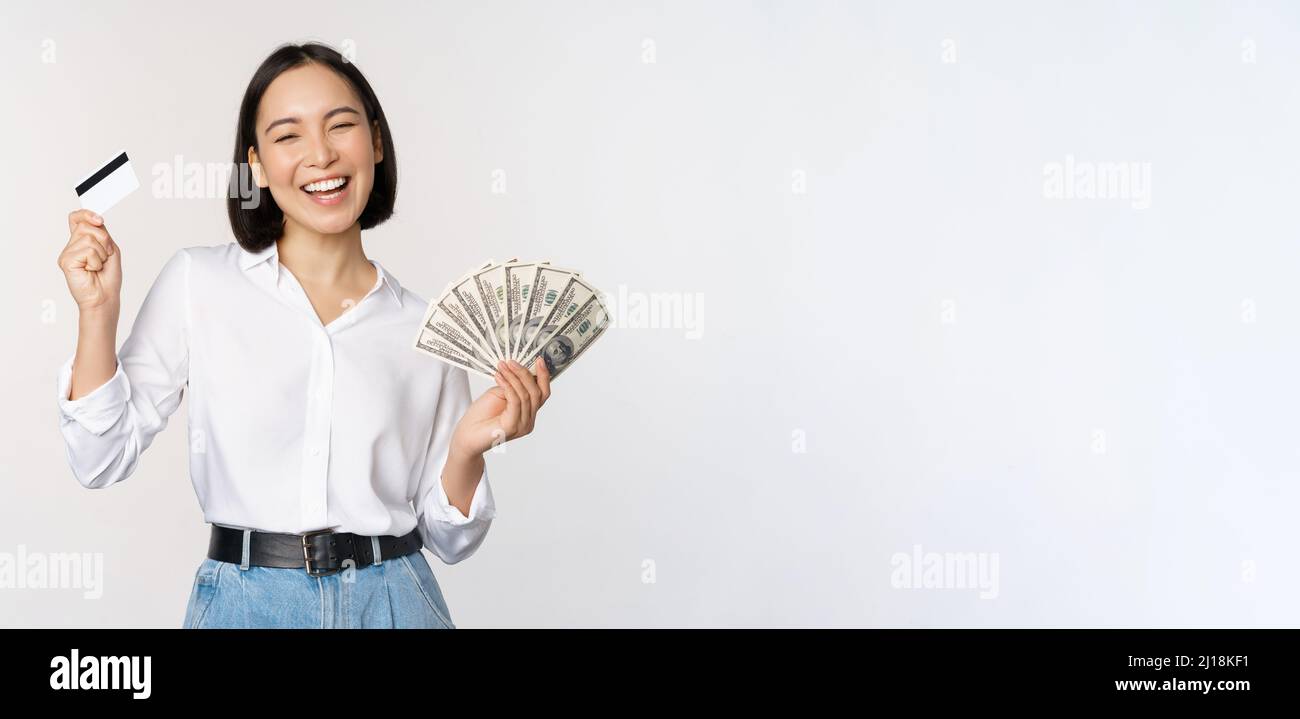 Happy korean woman holding credit card and money dollars, smiling and ...