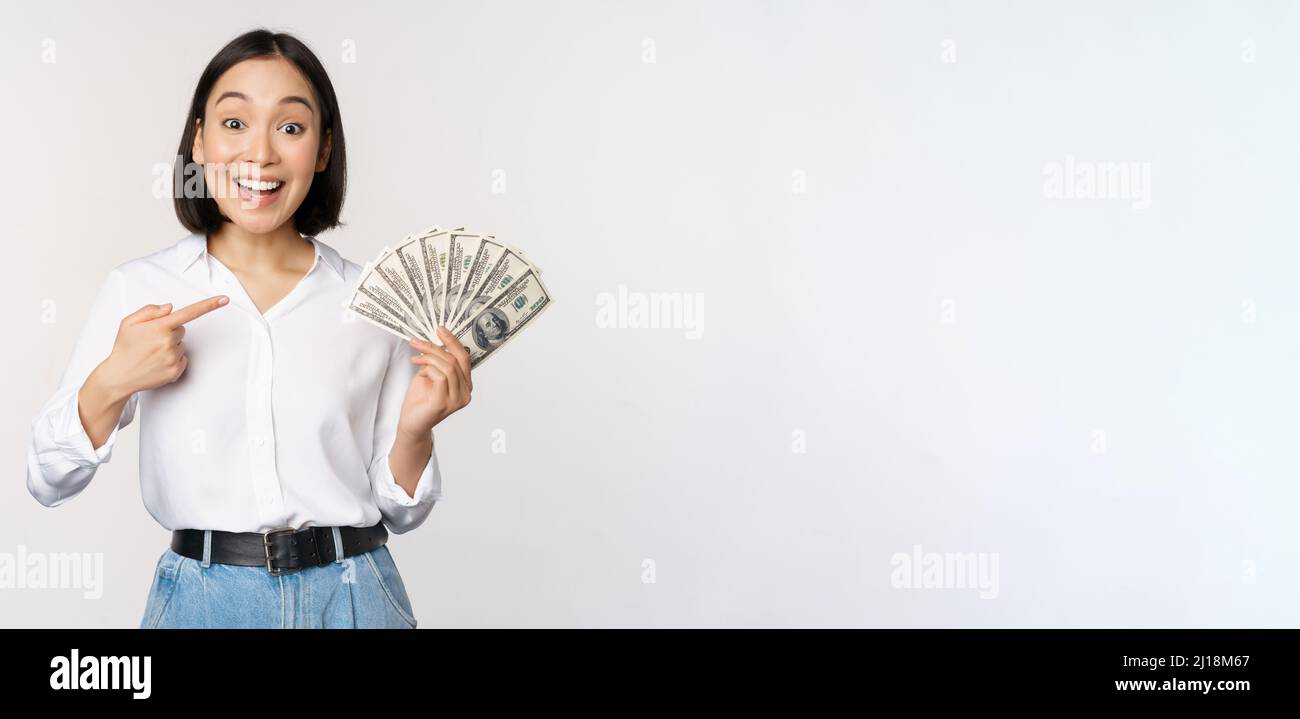 Portrait of young asian woman pointing at her money dollars, showing ...
