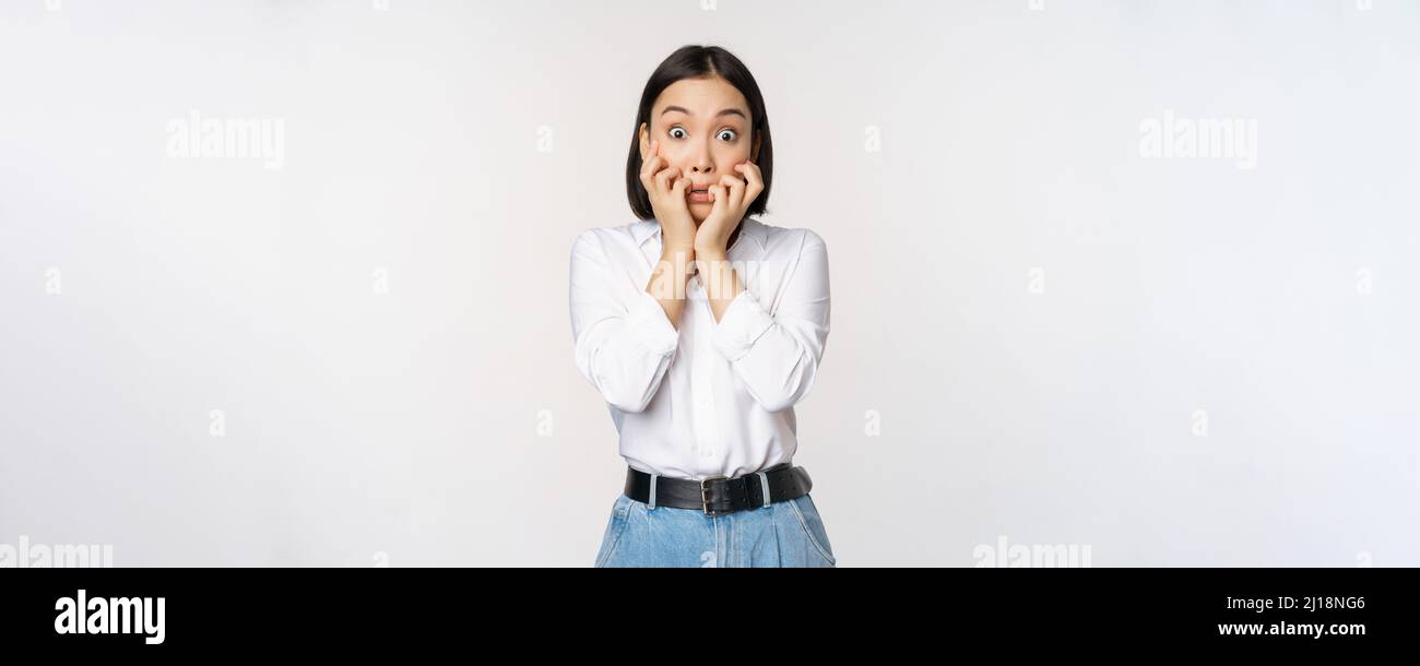 Portrait of scared asian woman watching smth scary, biting fingers on ...