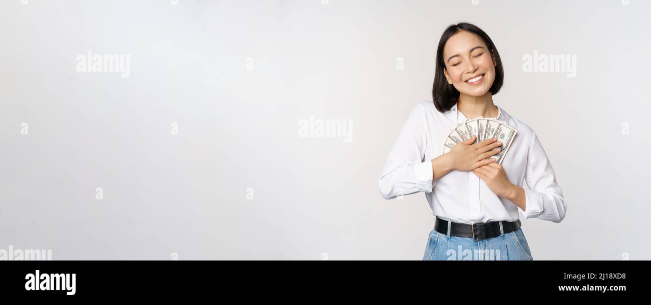Happy asian woman hugging money dollars and smiling satisfied, standing ...