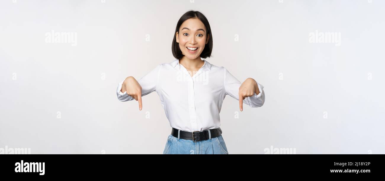 Portrait of young asian woman pointing fingers down and smiling ...