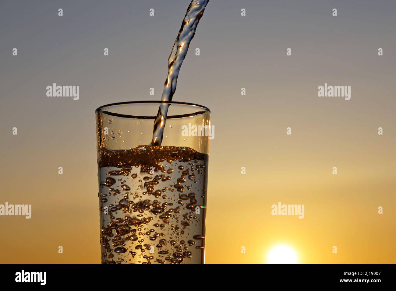 Clean water pouring into drinking glass on sunset sky background ...
