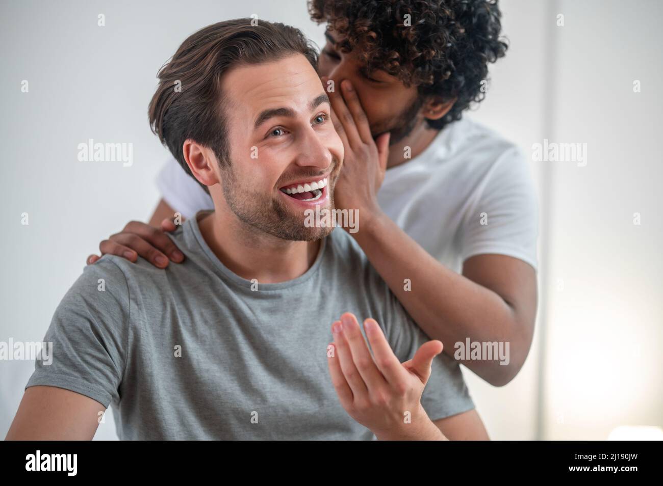 Indian man telling a secret to his pleased Caucasian boyfriend Stock ...