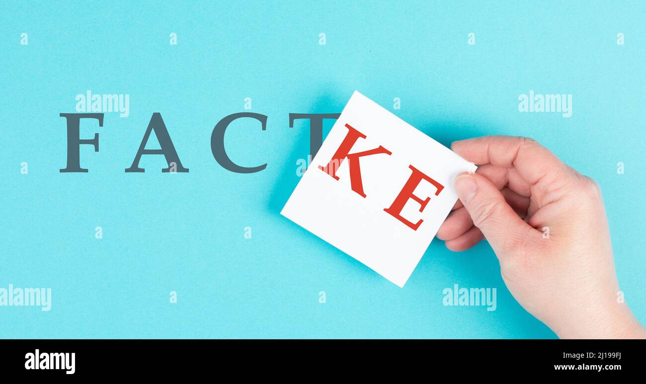 The word fact is standing on a paper, hand puts fake to the word, false ...