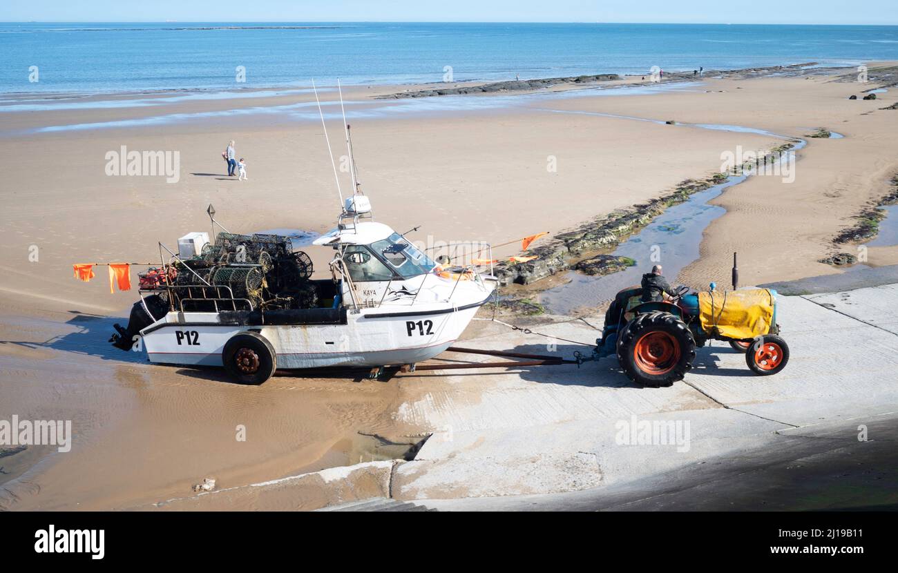Fisherman driving a tractor hauling his boat P12 Kaya up the slipway ...