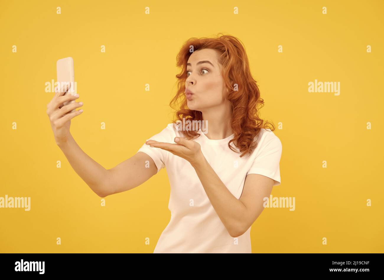 Girl make hand kissing gesture to camera phone yellow background ...