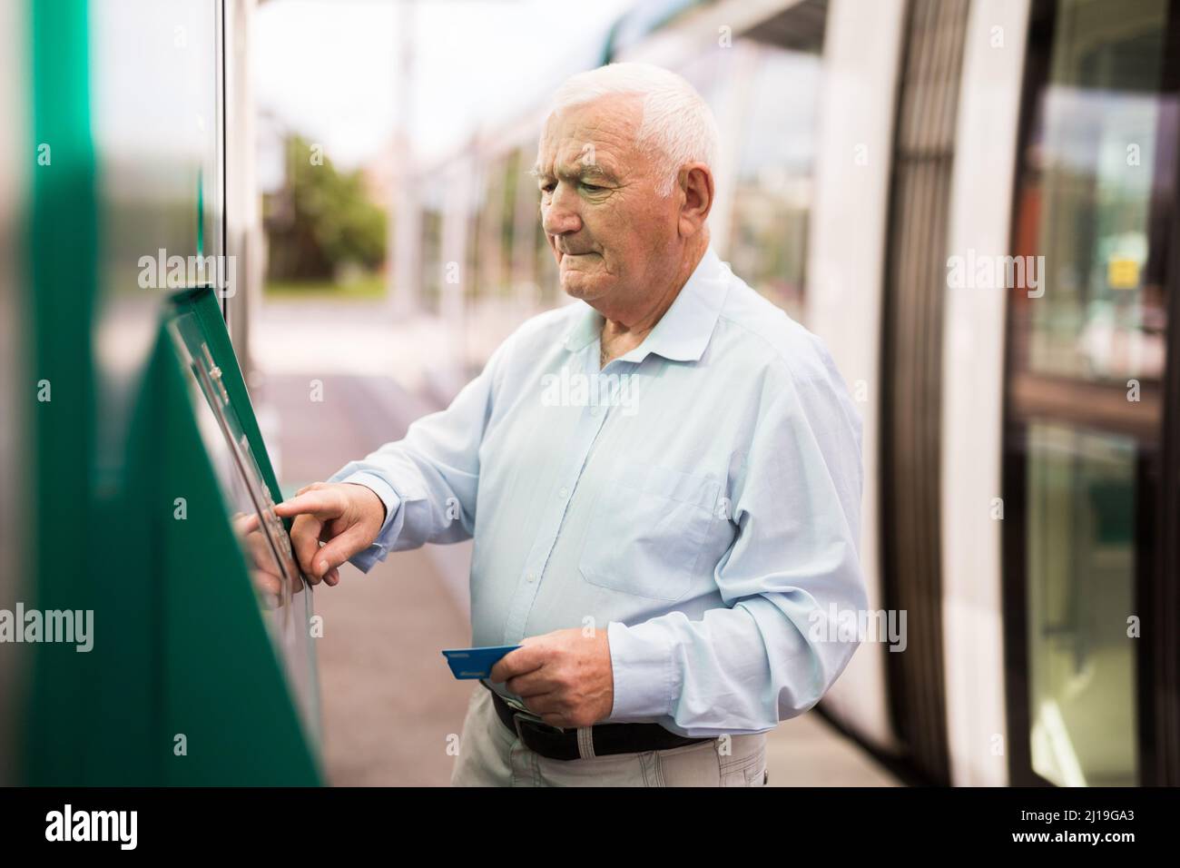 Senior man using ATM machine while standing on tram station Stock Photo ...