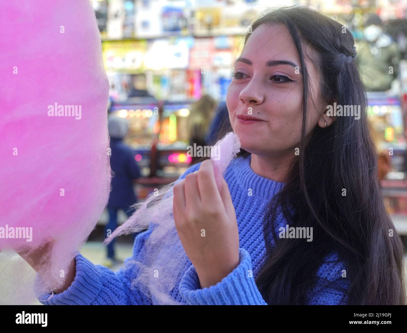 Girl looking as if she is enjoying while eating a cotton candy at night ...