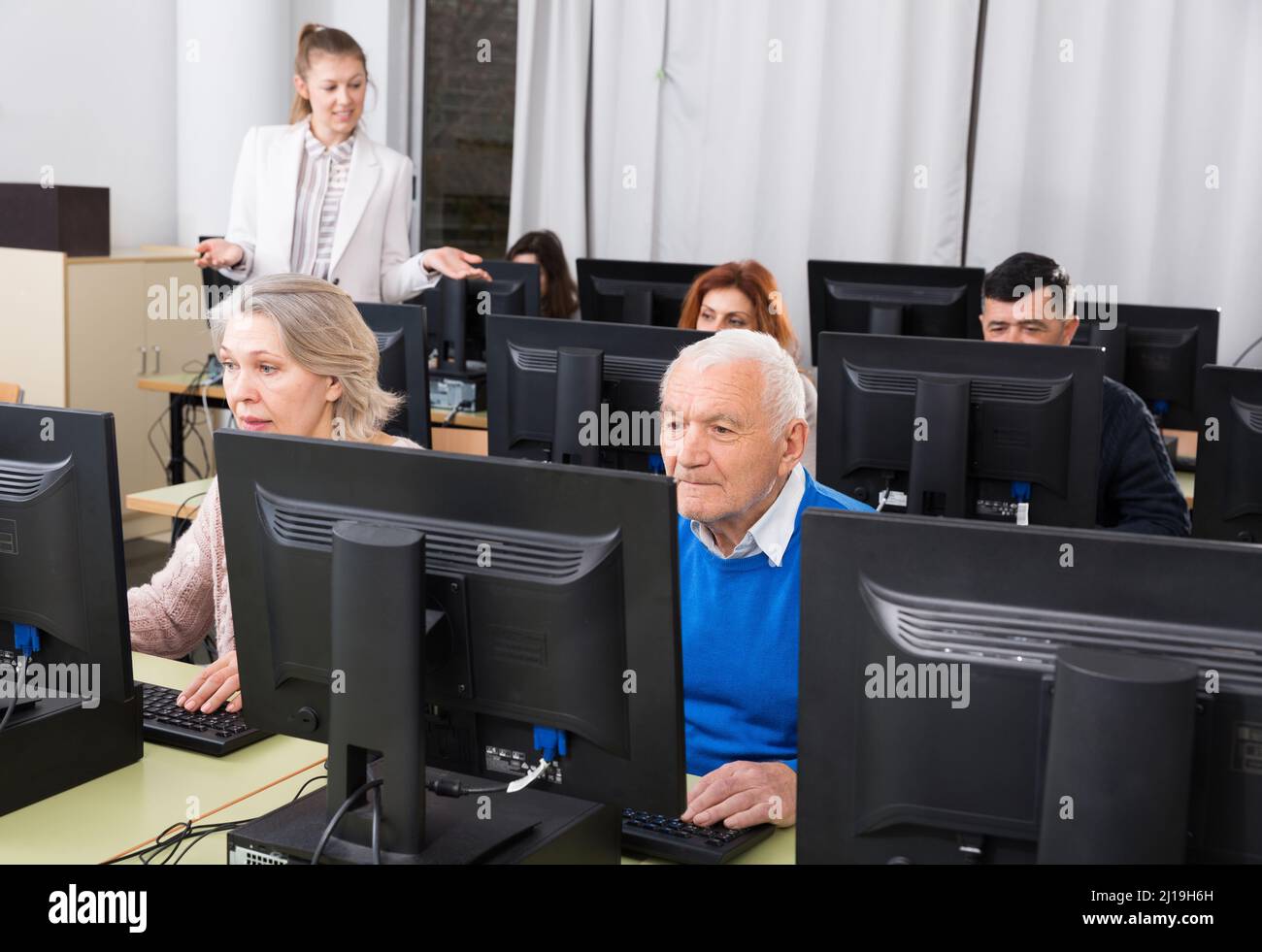 Elderly people working on computers with young teacher Stock Photo - Alamy