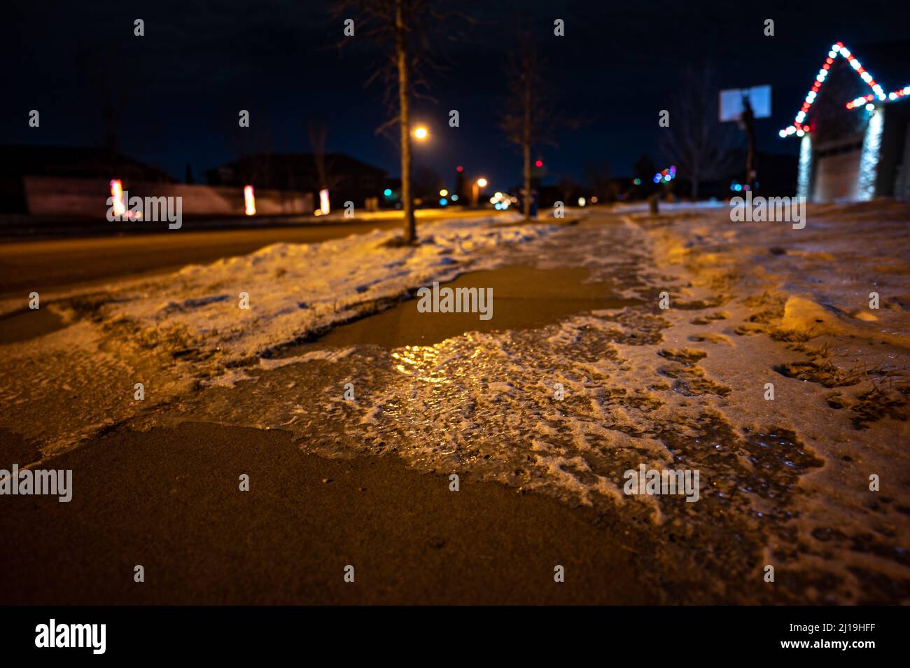 Ice and snow on a sidewalk at night with streetlight reflecting off the ...