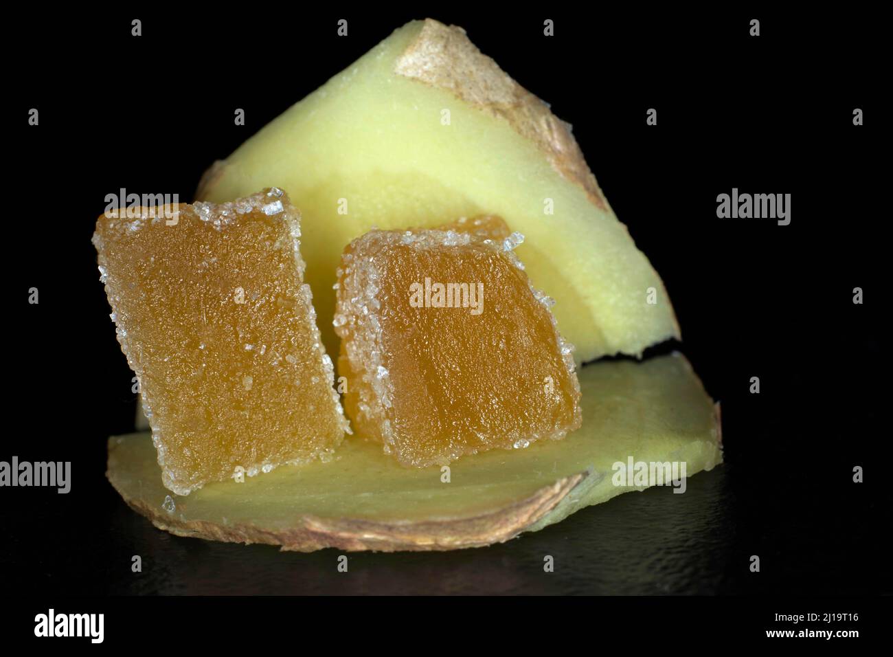 Two cubed candied ginger lies on a slice of fresh ginger, studio ...