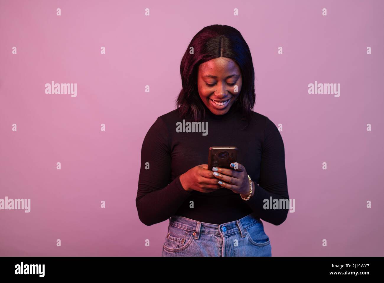A cheerful Nigerian woman texting with her phone isolated on pink ...