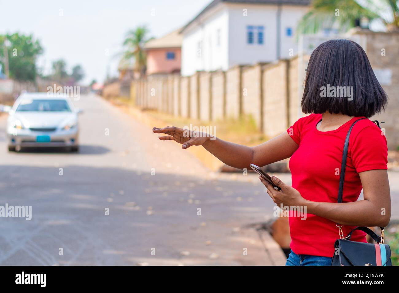 A beautiful Nigerian woman holding a phone while trying to hail a taxi ...