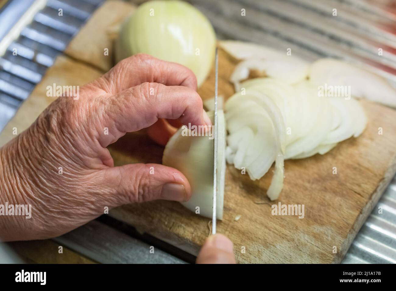 Old woman granny cutting onion in kitchen with knife and wooden board ...
