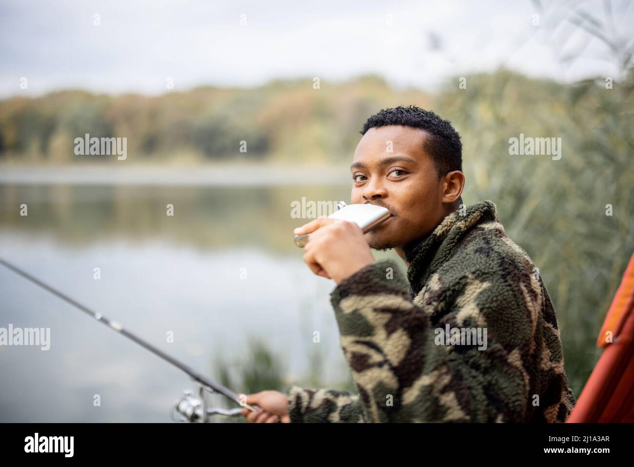 Man drinking from flask while fishing Stock Photo - Alamy