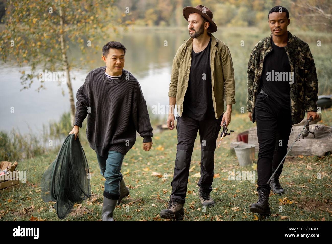 Multiracial male friends walking with fishing equipment in nature ...