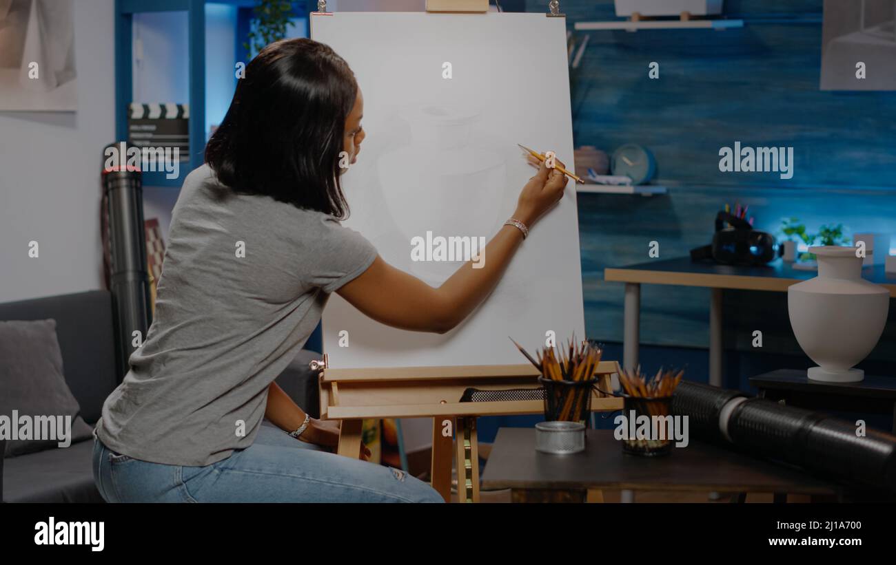 Artist of african american ethnicity drawing vase on white canvas with ...
