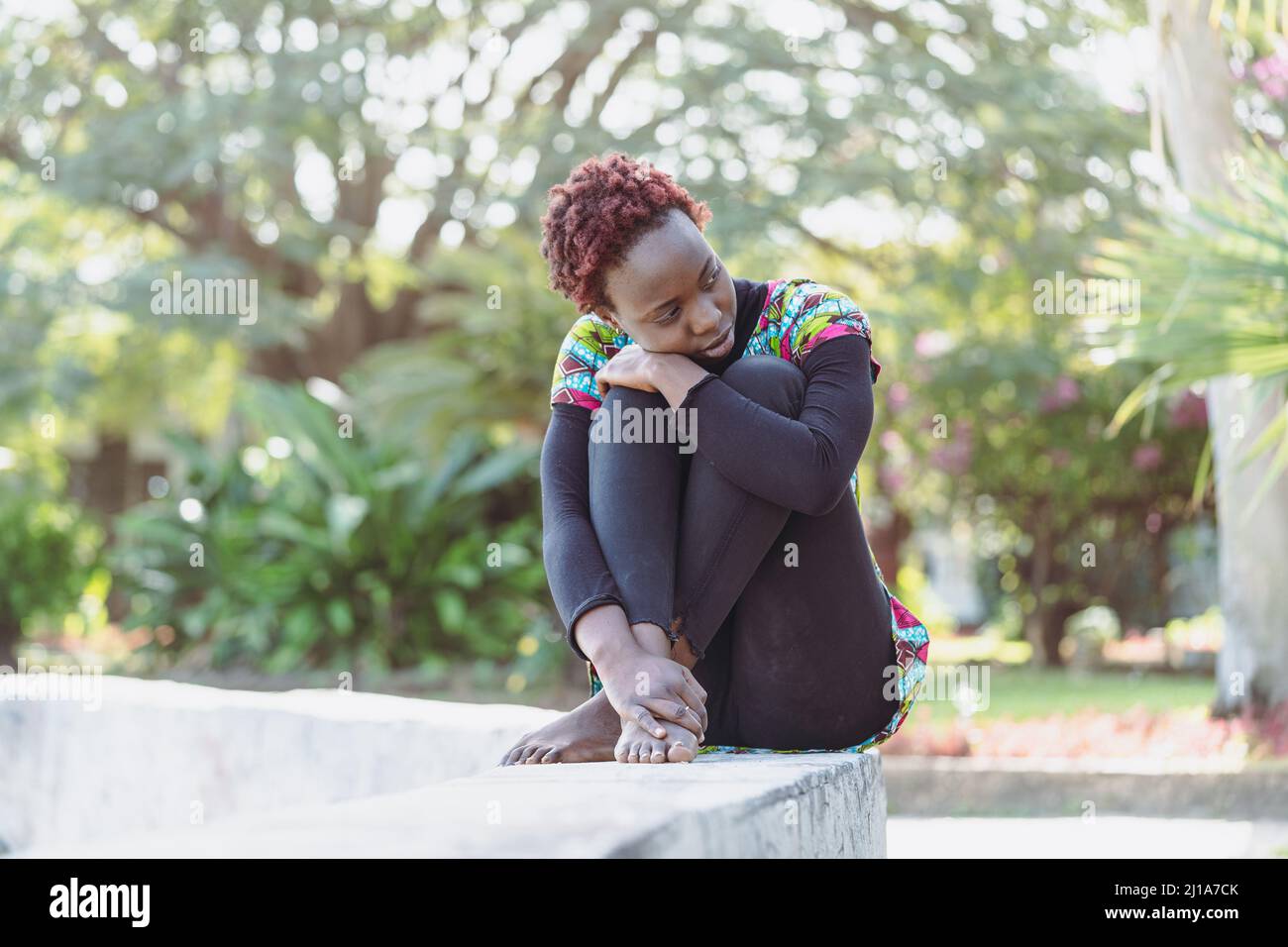 Melancholic young African teenage girl, sitting on a wall with her arms ...