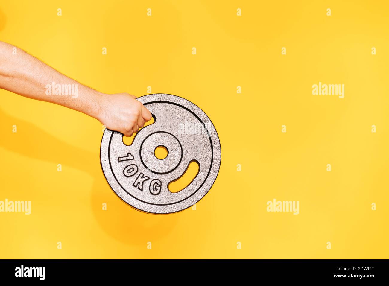 Hand holds ten-kilogram barbell dumbbell against yellow background ...