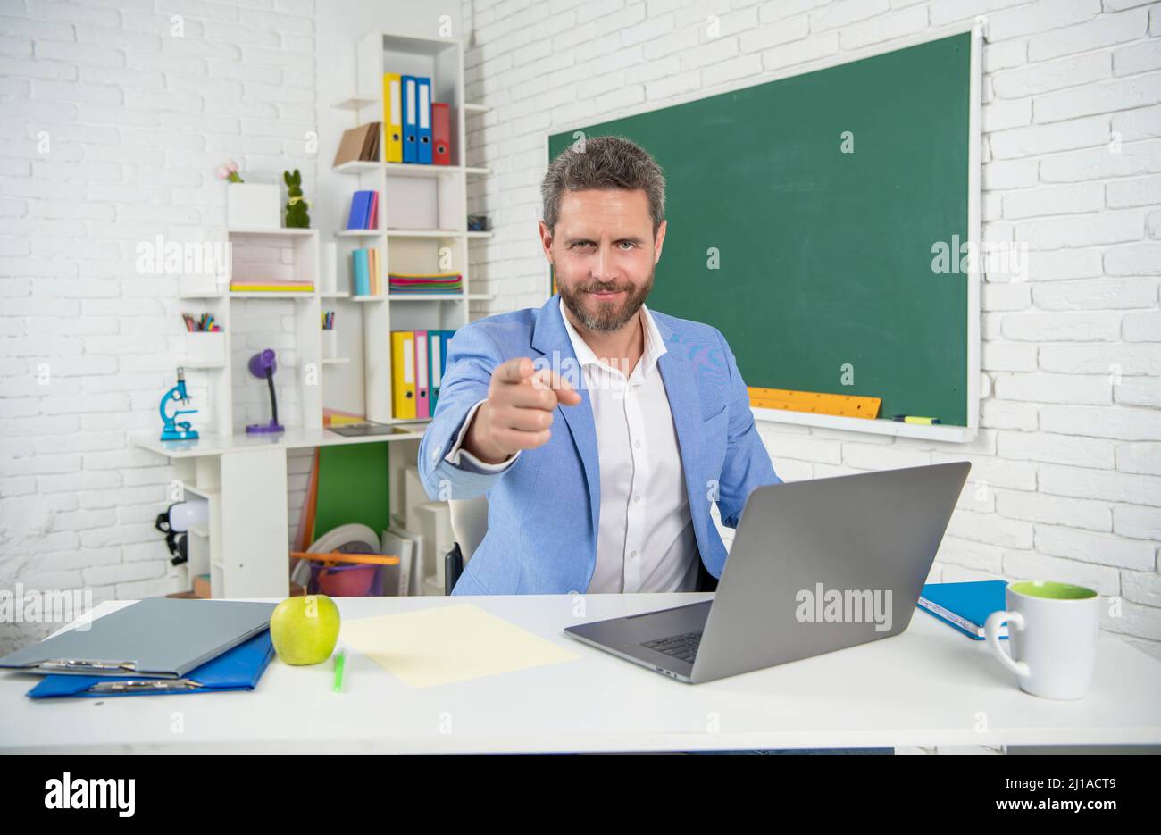 smiling school teacher in classroom with computer at blackboard ...