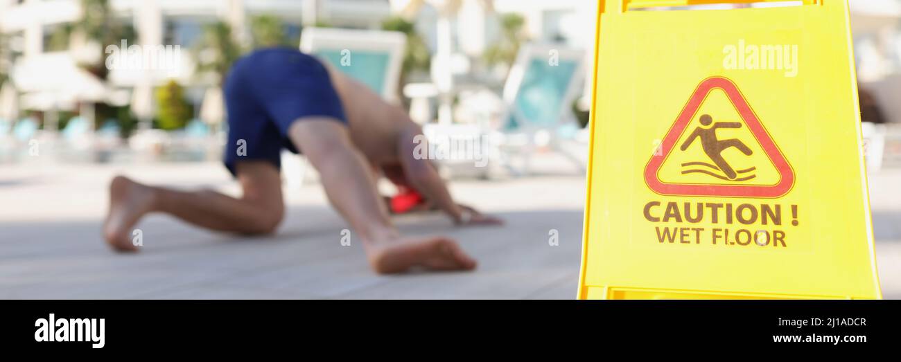 Yellow sign with warning caution wet floor standing near falling man ...