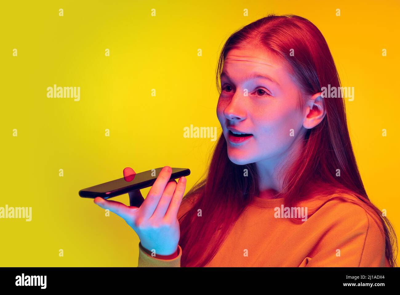 Portrait of teen girl recording voice message on her phone isolated ...