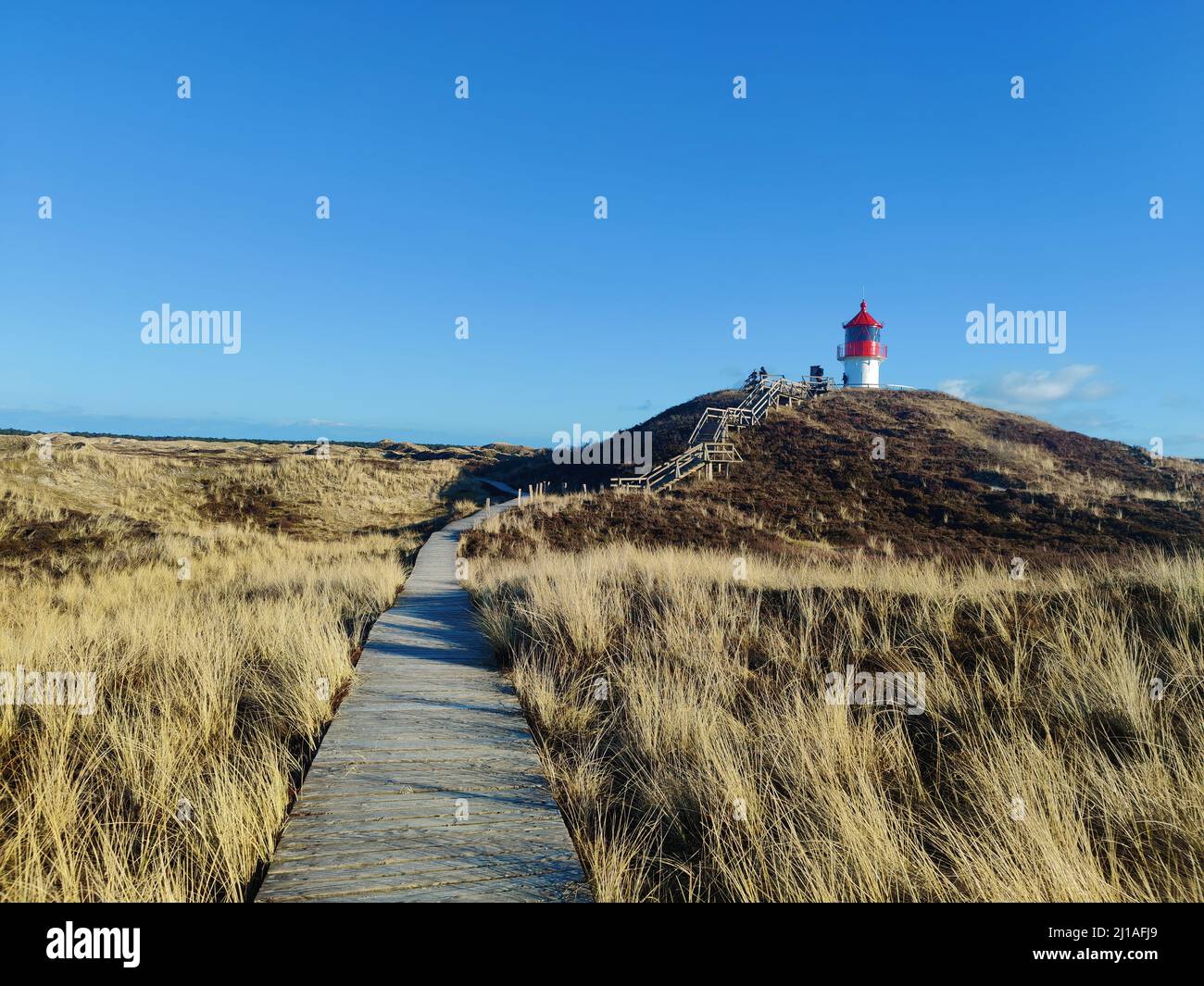 The beautiful coastline shot of a wooden pier to a small lighthouse in ...