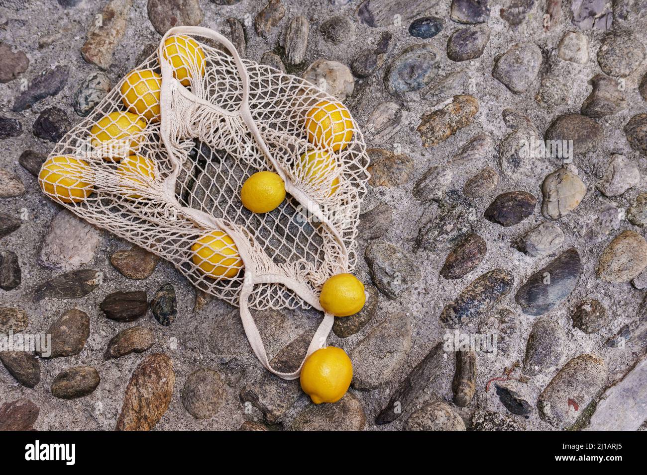 Net bag with a heap of fresh lemons lying on the cobblestone Stock ...