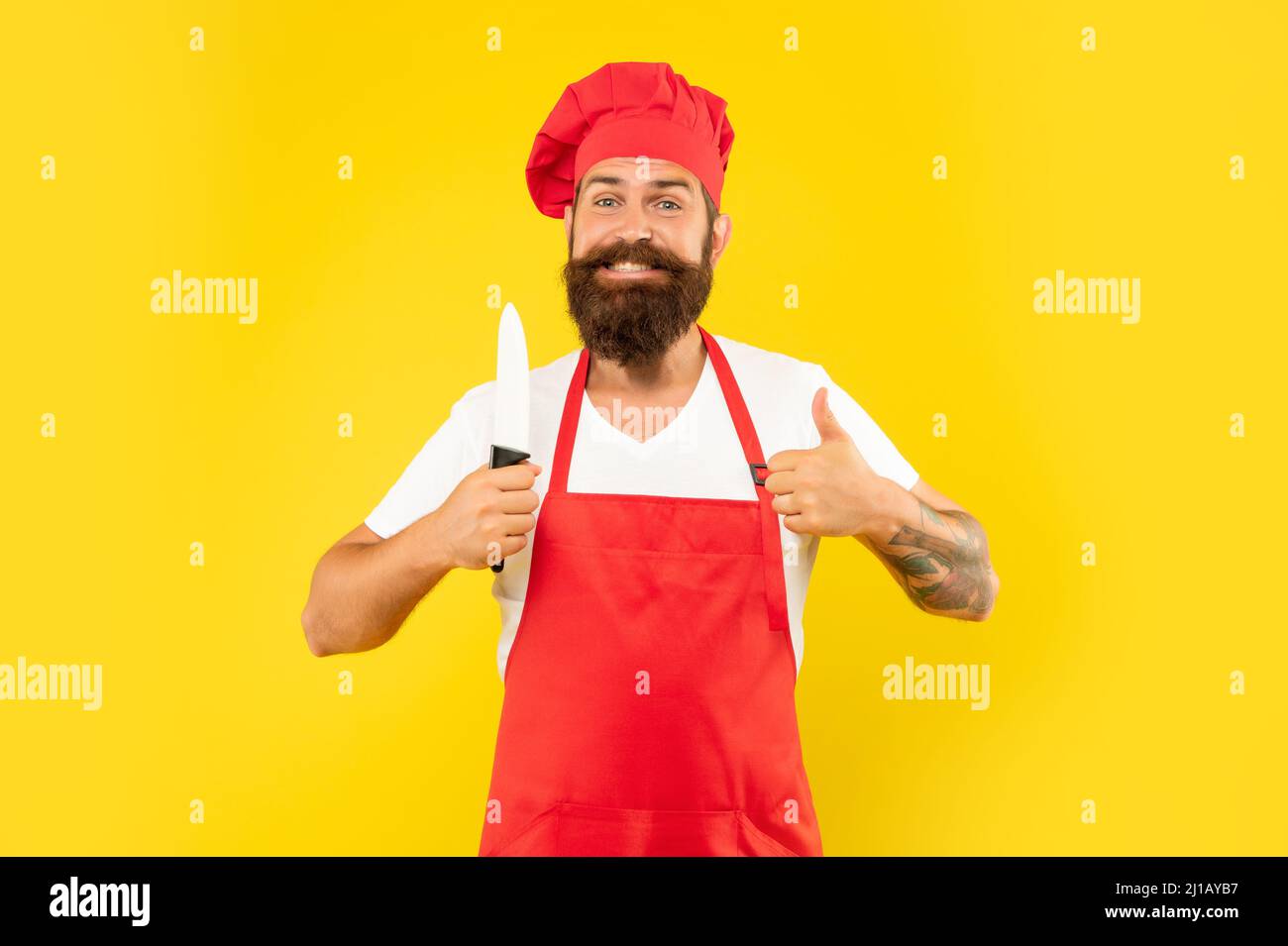 Happy man in red apron and toque giving thumb holding chefs knife ...