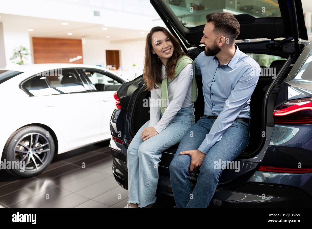 a young married couple in a car dealership chooses a car sits with a ...