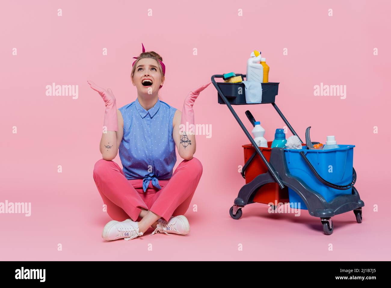 full length of crying young woman in rubber gloves sitting near ...