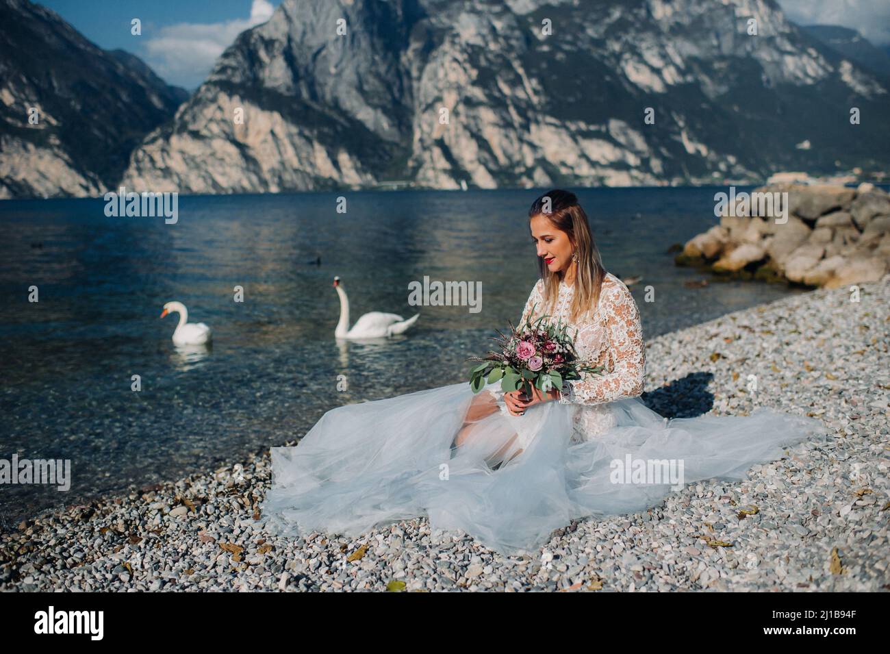 a girl in a smart white dress is sitting on the embankment of lake ...