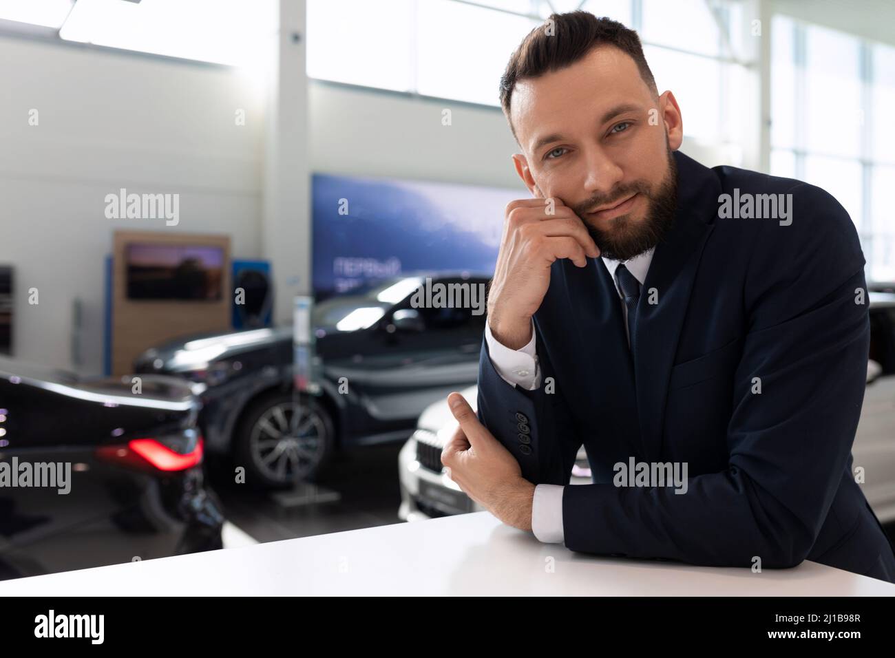 portrait of an employee of a car dealership in the showroom against the ...